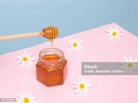 꿀벌 꿀은 나무 주걱에서 유리 항아리에 물방울 분홍색과 파란색 배경 데이지 유용한 농산물 건강관리와 의술에 대한 스톡 사진 및