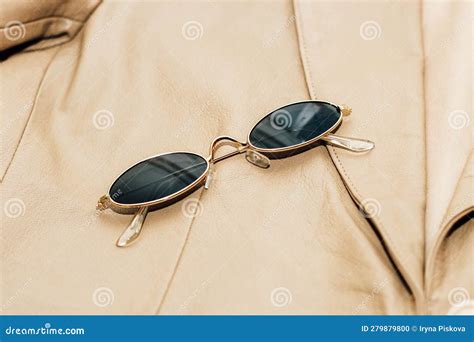 Gold Rimmed Sunglasses On The Texture Of A Brown Leather Jacket
