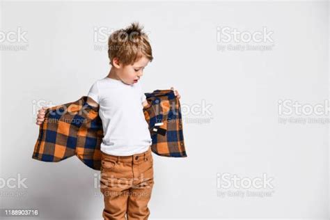 티셔츠와 청바지에 어린 아이 소년은 흰색에 바닥에 그것을보고 자신의 격자 무늬 셔츠를 벗고 열고 들고있다 T 셔츠에 대한 스톡 사진 및 기타 이미지 Istock