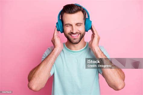 평화로운 긍정적 인 현대 남자가 파란색 무선 헤드셋을 듣고 음악을 즐길 수 노래 멜로디 가까운 눈을 느끼는 즐거움을 느끼는 캐주얼 스타일의 옷을 파스텔 색상 배경을 통해