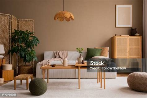 모듈식 소파 나무 커피 테이블 등나무 사이드보드 녹색 베개 램프 갈색 푸프 베이지색 깔개 식물 및 개인 액세서리가 있는 거실의