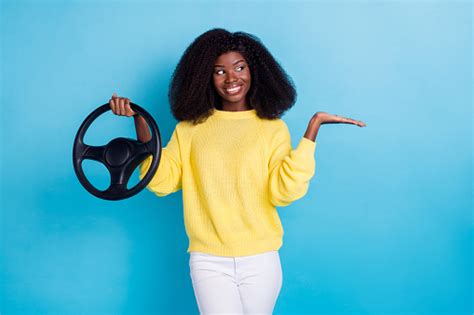 매력적인 갈색 머리 낙관적 인 소녀 노란색 스웨터가 파란색 배경에 고립 된 빈 공간을 지시하는 스티어링 휠을 잡고 사진