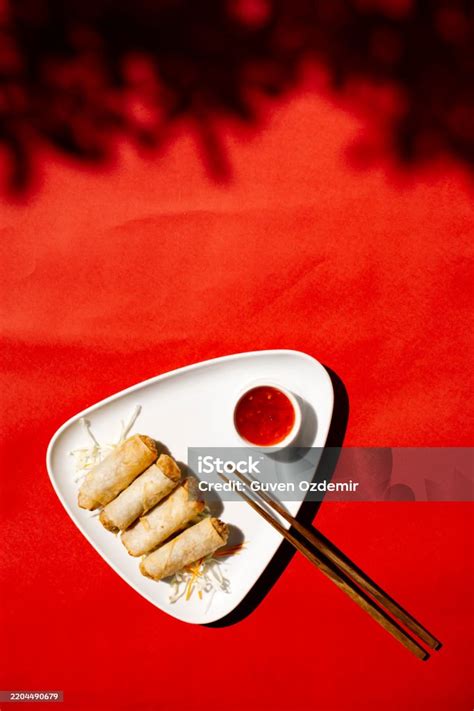 예술적 그림자가 있는 생생한 빨간색 배경에 빨간 스위트 칠리 디핑 소스와 나무 젓가락이 있는 흰색 삼각형 접시에 배열된 바삭한 황금빛 춘권의 평면도 아시안 애피타이저 컨셉