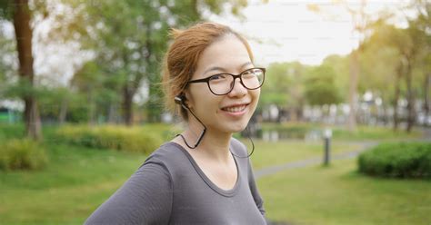 회색 운동복을 입은 행복한 젊은 아시아 여성은 아침에 야외에서 이어폰으로 음악을 들으며 웃고 있다 공원에서 여성 운동 건강 관리 및 스포츠 개념입니다 공간을 복사합니다