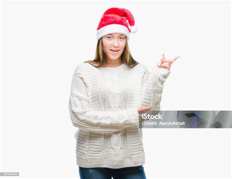 젊은 아름 다운 백인 여자 얼굴에 큰 미소와 함께 고립 된 배경 위에 크리스마스 모자를 쓰고 카메라를 보고 옆에 손 및 손가락으로 가리키는 가리키기에 대한 스톡 사진 및