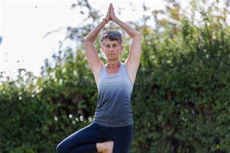A Middle Aged Woman Practicing Yoga Barefoot Outside In A Grassy Park
