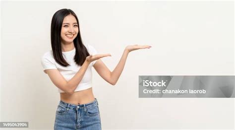 흰 셔츠를 입은 아름다운 미소 짓는 행복한 젊은 아시아 여성 매력적인 여성 아가씨는 고립된 흰색 배경에 무언가를 들고 손바닥을 위로 올립니다 아시아 귀여운 예쁜 사람들이