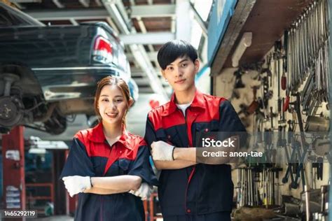 아시아 자동차 엔지니어 사람들은 정비사 차고에서 헬멧 작업을 착용합니다제복을 입은 젊은 자동차 정비사는 카메라를 보고 웃으며