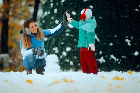 Mother And Daughter Making High Five Gesture Building A Snowman Stock
