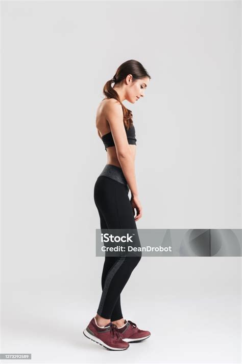 회색 배경위에 고립 된 프로필에 서있는 카메라에 포즈를 취하는 포니 테일의 머리카락을 가진 스포티 한 갈색 머리 여성의 전체 길이 사진 강사에 대한 스톡 사진 및 기타