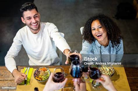 레스토랑에서 친구들과 함께 건배하는 젊은 커플 곱슬머리를 한 사이즈 소녀가 카메라를 바라보며 레드 와인 한 잔을 들고 미소를 짓고 있다 20 29세에 대한 스톡 사진 및