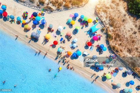 모래 해변에 화려한 우산의 공중 전망 여름에 일출에 푸른 바다에서 수영하는 사람들 사르데냐 이탈리아 맑은 푸른 물이 있는 열대 풍경 여행과 휴가 상단 드론 보기