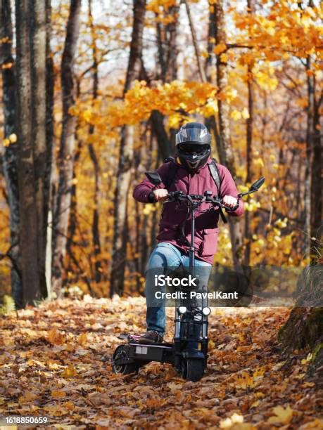 한 젊은이가 가을 공원에서 스쿠터를 탄다 강력한 현대식 전기 운송 수단 단풍잎의 가을 길 전기 스쿠터에 대한 스톡 사진 및 기타 이미지 Istock