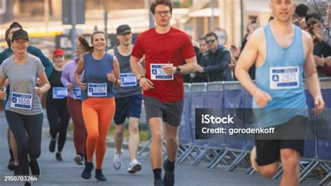 낮 동안 도시에서 마라톤을 달리는 다양한 그룹의 사람들 결승선에 도달하기 위해 경쟁하는 남녀 주자를 응원하고 응원하는 가족과 친구들 1개월에 대한 스톡 사진 및 기타 이미지