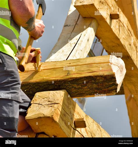 Carpenter Inserting A Wedge In A Joint Locking Peg In A New Build Traditional Medieval Oak