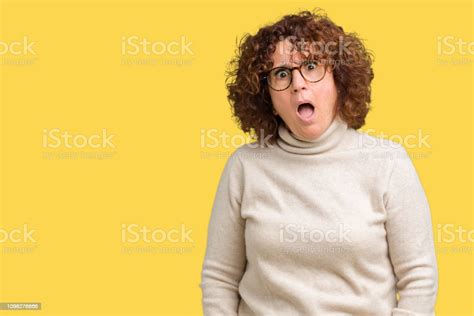 아름 다운 중간 어른 수석 입고 여자 터틀 넥 스웨터와 안경 충격 얼굴에 고립 된 배경 위에 보고 회의 냉소 오픈 입으로 놀 스페인 포르투갈 민족에 대한 스톡 사진 및 기타