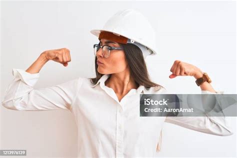 헬멧과 안경을 쓰고 고립된 흰색 배경 위에 팔을 쓰고 자랑스럽게 웃고 있는 젊은 아름다운 건축가 여성 피트니스 개념입니다 갈색 머리에 대한 스톡 사진 및 기타 이미지