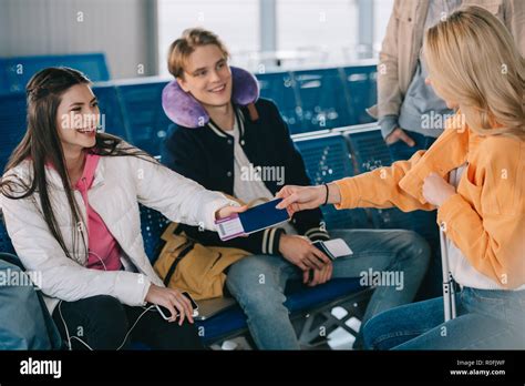 Friends Holding Passport With Boarding Pass While Waiting In Airport