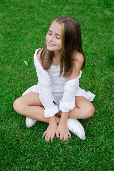 Pretty Tween Girl In White Clothes Sitting On Green Grass Outside In