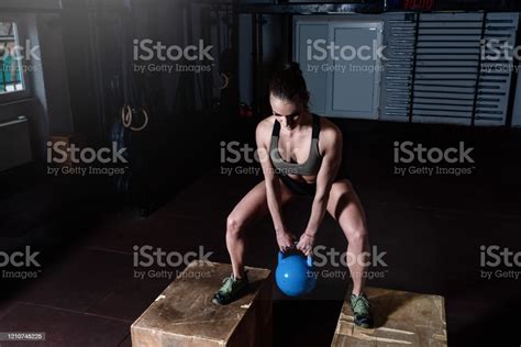체육관에서 하드 코어 크로스 강도 운동 훈련을위한 무거운 케틀벨과 두 개의 나무 점프 상자에 깊은 쪼그리고 딥을하고 강한 다리를 가진 젊은 땀이 근육 맞는 소녀 20 29