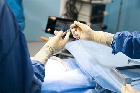 Medic In Operating Room Passing Surgical Instrument To Colleague