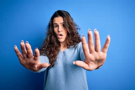 고립 된 배경위에 파란색 캐주얼 스웨터를 입고 곱슬 머리를 가진 젊은 아름다운 여성은 손바닥 화가 좌절 표정으로 중지 제스처를하고 격노한에 대한 스톡 사진 및 기타 이미지