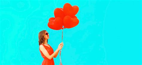 파란색 배경에 선글라스를 착용한 빨간 하트 모양의 풍선무리와 함께 아름다운 행복한 미소 짓는 젊은 여성 25 29세에 대한 스톡 사진 및 기타 이미지 Istock