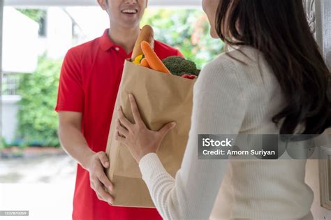 종이 봉투나 종이 통으로 신선한 음식을 받는 여성은 문 앞에서 배달원으로부터 배달원으로부터 우편 배달 음식 집에서 받는 사람에게 야채 음식 배달 온라인 쇼핑 및 운송 주기에