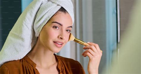 머리에 수건을 얹은 현대 젊은 여성이 거울 앞에 서서 얼굴에 화장 파운데이션을 바르고 있다 사진 Unsplash의 라이프 스타일 이미지