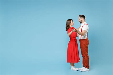 파스텔 블루 컬러 배경 스튜디오 초상화에서 서로 고립 된 서로를 보고 춤을 추는 흰색 빨간 옷을 입은 젊은 부부 두 친구 남자 여성이 미소짓는 전체 길이 세인트 발렌타인