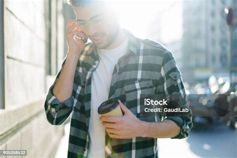 Gropped 유행 안경 전화를 통해 통신 하 고 신중 하 게 도시의 설정에서 봄 산책 중 듣고 있는 남자의 이미지 선샤인 시티에서 산책 하는 동안 거리에서 자유 시간을