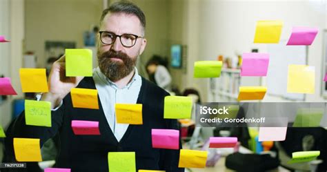 컬러풀한 노트와 계획이 유리와 일하는 사람들 뒤에 매달려 있는 사려 깊고 창의적인 에이전시에서 미소짓는 남자의 초상화 개념에 대한 스톡 사진 및 기타 이미지 Istock