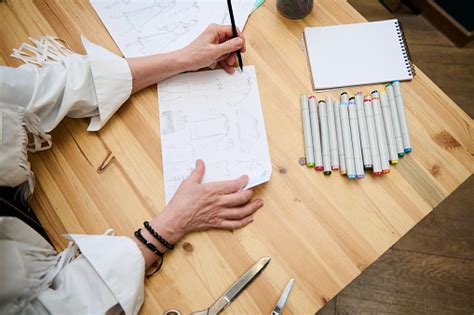 여성 패션 디자이너 드레스 메이커 그녀의 창조적 인 디자이너 사무실의 나무 테이블에 연필과 수채화 마커와 옷에 대한 스케치를 그리기 드레스 메이커의 클로즈업 보기 재단사에