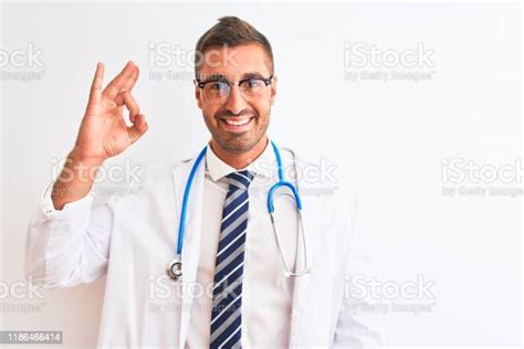 손과 손가락으로 확인 기호를하고 긍정적 인 미소 고립 된 배경 에 청진기를 입고 젊은 잘 생긴 의사 남자 성공적인 식입니다 건강관리와 의술에 대한 스톡 사진 및 기타 이미지