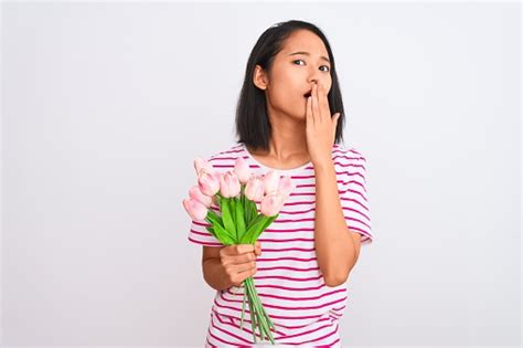 장미의 꽃다발을 들고 있는 젊은 중국 여성은 실수 두려움의 표정 침묵 비밀 개념에 대한 수치심으로 충격을 받은 손으로 고립 된 흰색 배경 커버 입 위에 서 있습니다 가리기에