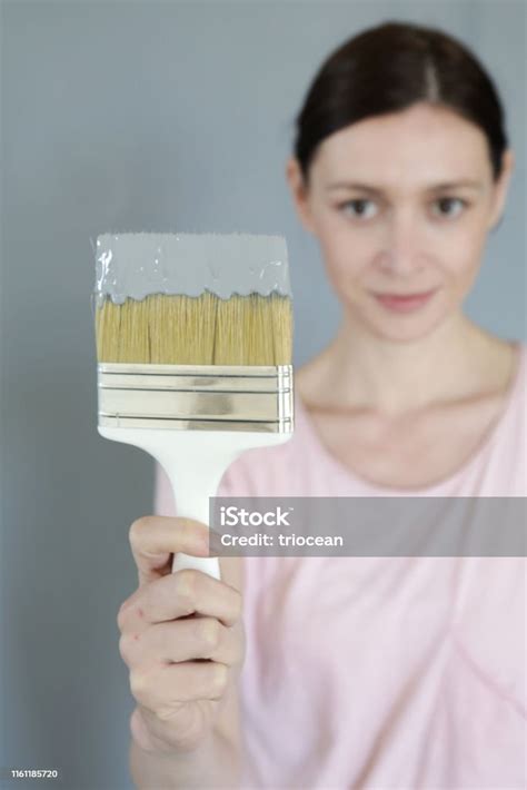 페인트 브러시를 들고 있는 젊은 여성의 초상화 흰 벽에 회색 페인트로 칠한 여성 Diy에 대한 스톡 사진 및 기타 이미지