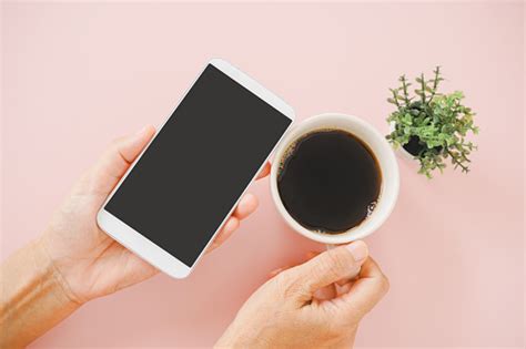 터치 스크린에 클리핑 경로와 흰색 휴대 전화를 들고 노인의 손 다른 달콤한 핑크 배경에 뜨거운 커피 한 잔을 개최 Brand Name Smart Phone에 대한 스톡 사진