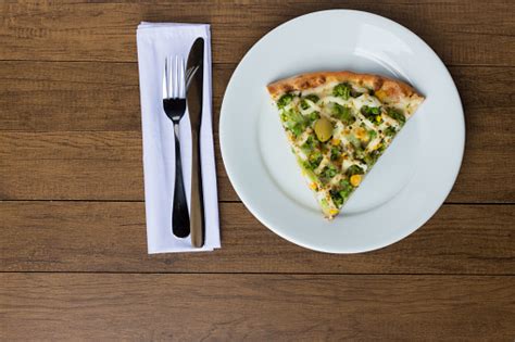 브로콜리 피자는 나무 판에 제공됩니다 모짜렐라 브로콜리 옥수수 완두콩 올리브로 구운 제품입니다 접시에 담긴 피자 조각 포크와 칼 수평 상단 사진입니다 길거리 음식에 대한