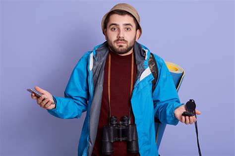 잃어버린 여행자는 라일락 배경위에 고립 된 포즈를 취하고 파란색 재킷 셔츠 및 모자를 쓰고 무기력한 표정을 가진 남자 숲에서 시간을 보내는 동안 남성이 길을 잃었습니다