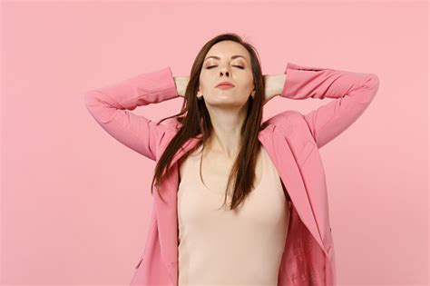 스튜디오에서 파스텔 분홍색 벽 배경에 고립 된 머리 뒤에 손을 잡고 눈을 유지 재킷을 입고 편안한 여자의 초상화 사람들은 진심으로 감정 라이프 스타일 개념입니다 복사 공간을