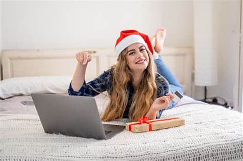 산타 클로스 모자를 들고 신용 카드 선택 하 고 온라인 쇼핑 및 겨울 휴가에 인터넷 판매 및 신용 카드 시설 흥분 집에서 노트북을 사용 하 여 크리스마스 선물을 구입 12