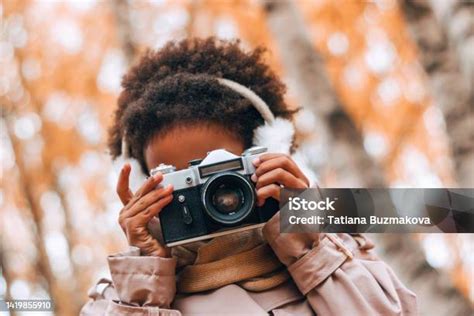 모피 헤드폰을 입은 귀여운 아프리카 계 미국인 소녀가 가을 공원에서 카메라로 사진을 찍습니다 다양성 가을 개념 사진 촬영 이미지 캡처에 대한 스톡 사진 및 기타 이미지