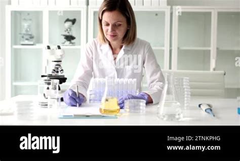 Lab Worker In Rubber Gloves Writes Analysis Of Laboratory Experiment Woman In Hospital Robe At