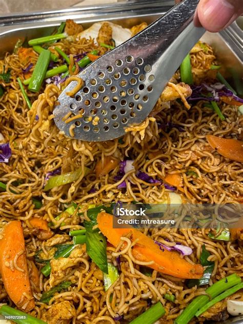 알아볼 수 없는 사람이 흰색 접시에 차우멘 볶음 튀김을 요리하는 전체 프레임 이미지 호텔 셀프 서비스 뷔페에서 스테인리스 스틸 케이터링 트레이에서 금속 서빙 집게와 함께