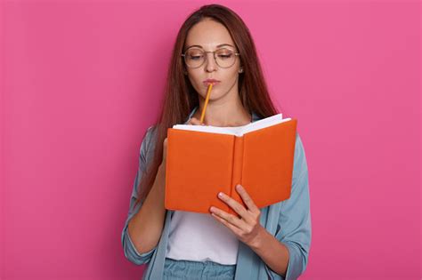 사려 깊은 표정으로 매력적인 여성의 수평 초상화 그녀의 작업에 대해 생각 뭔가를 계획 정장과 안경을 입고 핑크 스튜디오 배경 위에 고립 된 포즈 갈색 머리에 대한 스톡 사진