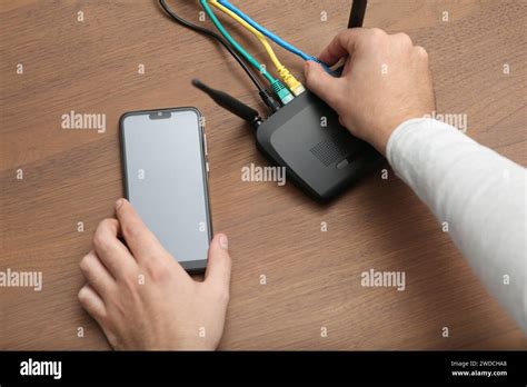 Man With Smartphone Connecting To Internet Via Wi Fi Router At Wooden