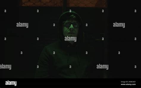 The Mysterious Hooded Handsome Hacker With Glasses In A Green Lit Abandoned Underground Room