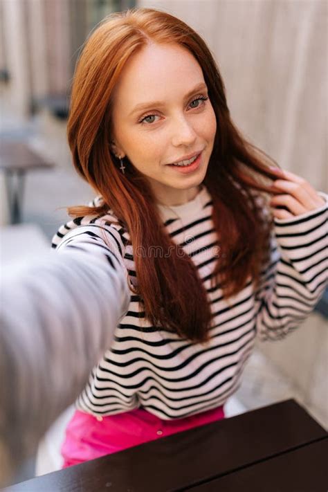 Vertical POV Portrait Of Pretty Redhead Female Taking Selfie On Smartphone Camera Sitting At