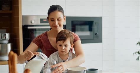 집에서 아들과 함께 아침을 먹으면서 유리잔에 우유를 붓는 젊은 어머니 사진 Unsplash의 세르비아 이미지