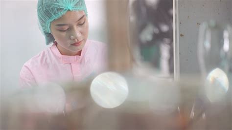 여성 식품 과학자 노동자 또는 영양사 또는 품질 관리 책임자는 헤어넷과 멸균 된 의복을 입고 공장의 생산 라인에서 병에 채워지는